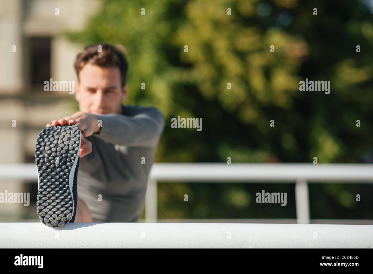 Flexibility and exercise. Muscular guy puts his foot on railing and ...