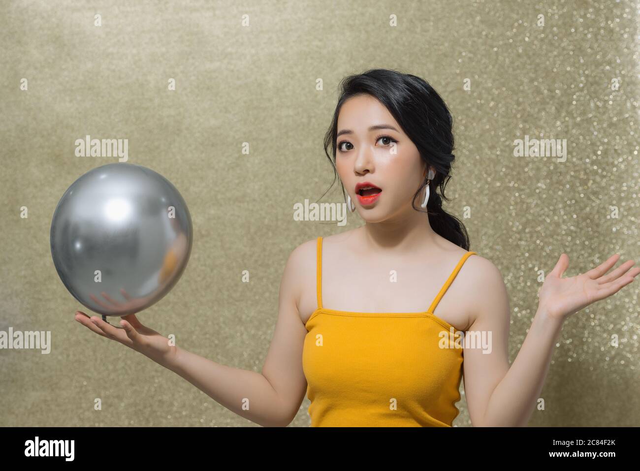 Cheerful young Asian woman with balloons laughing over gold background ...