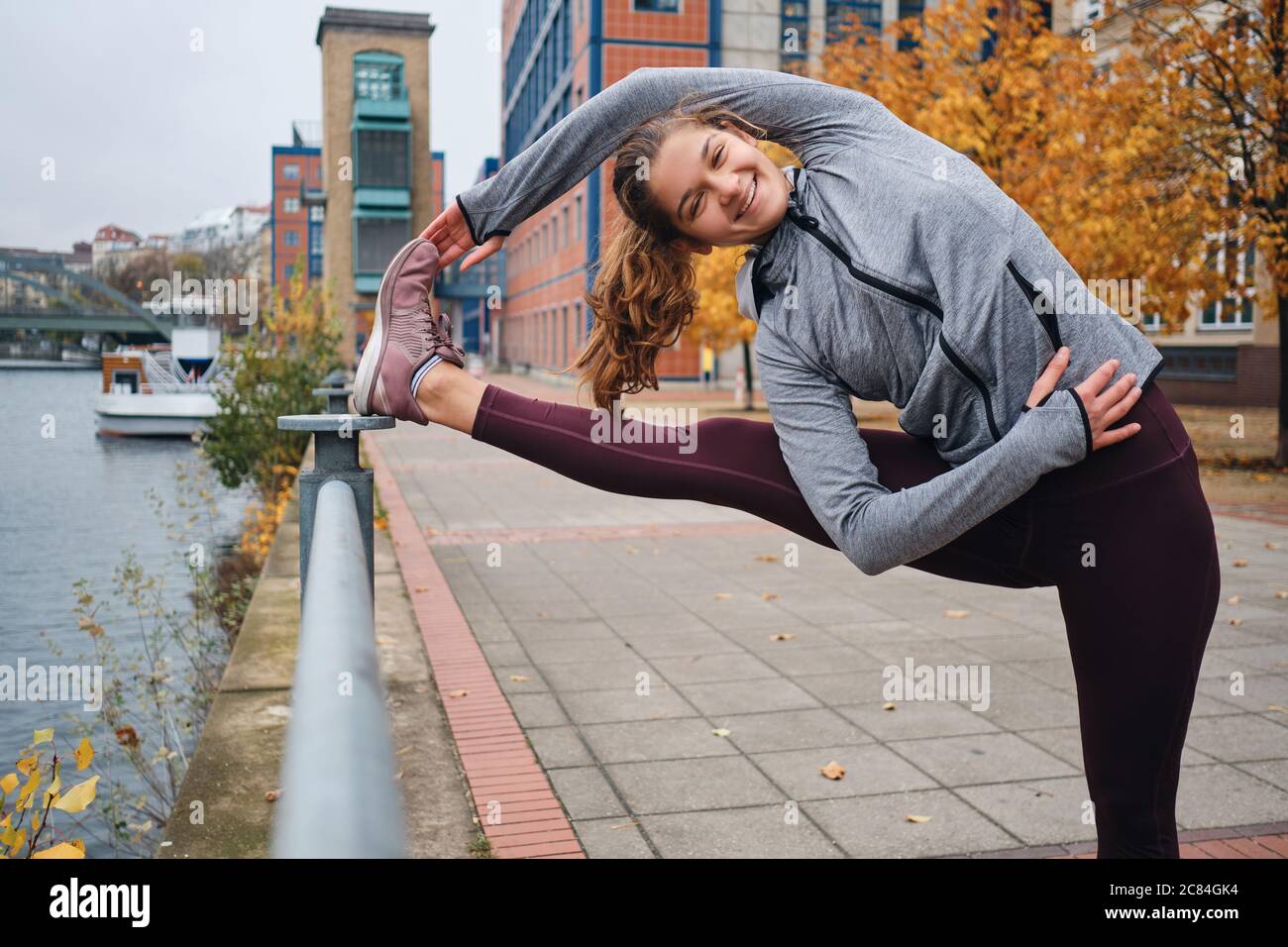 Pretty smiling sporty girl happily stretching during workout on city ...
