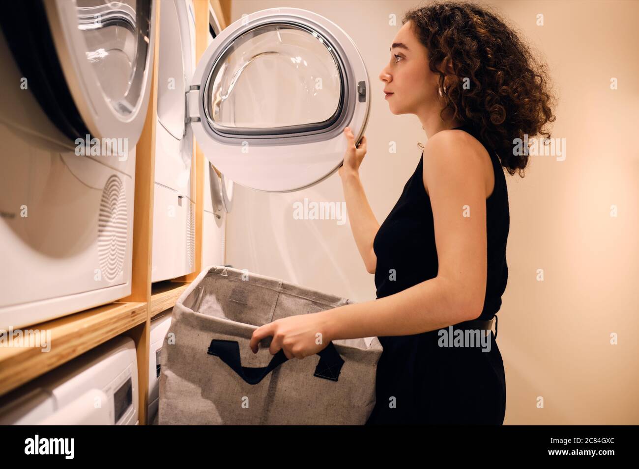 Side view of beautiful girl loading clothes into washing machine in ...