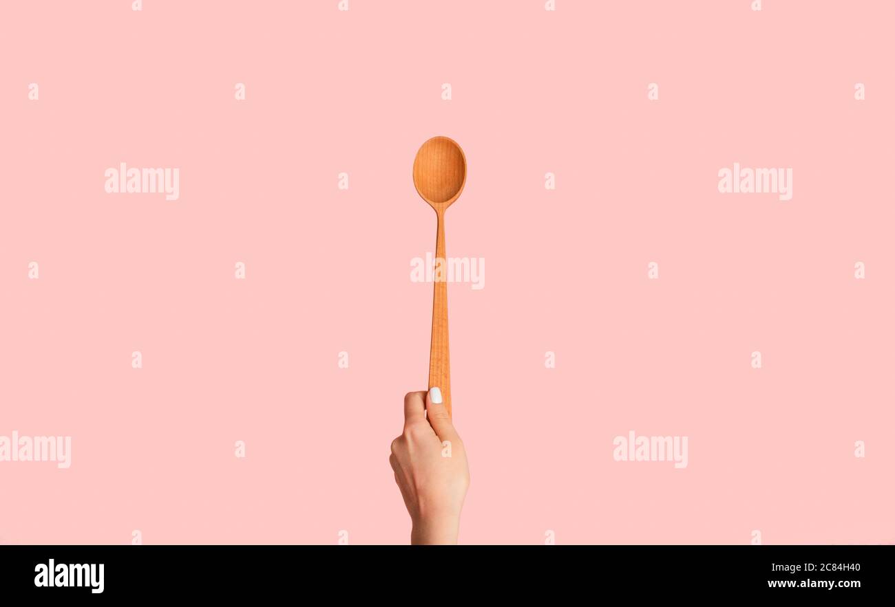 Millennial woman holding wooden spoon over pink background, close up ...