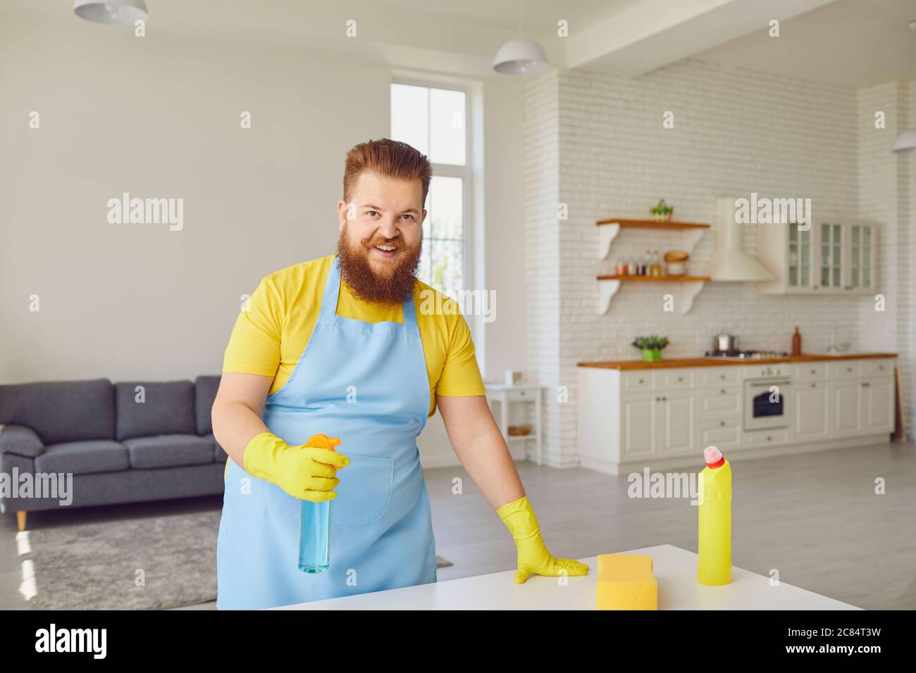 Funny fat man with a beard in an apron cleans the room in the house ...