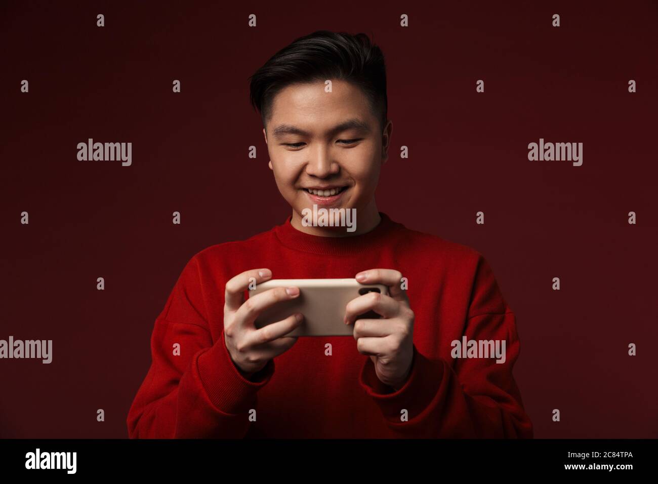 Image of joyful young asian man playing video game on mobile phone ...
