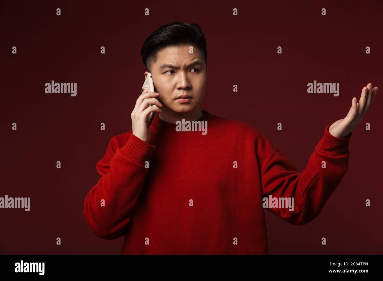 Image of displeased young asian man talking on mobile phone isolated ...