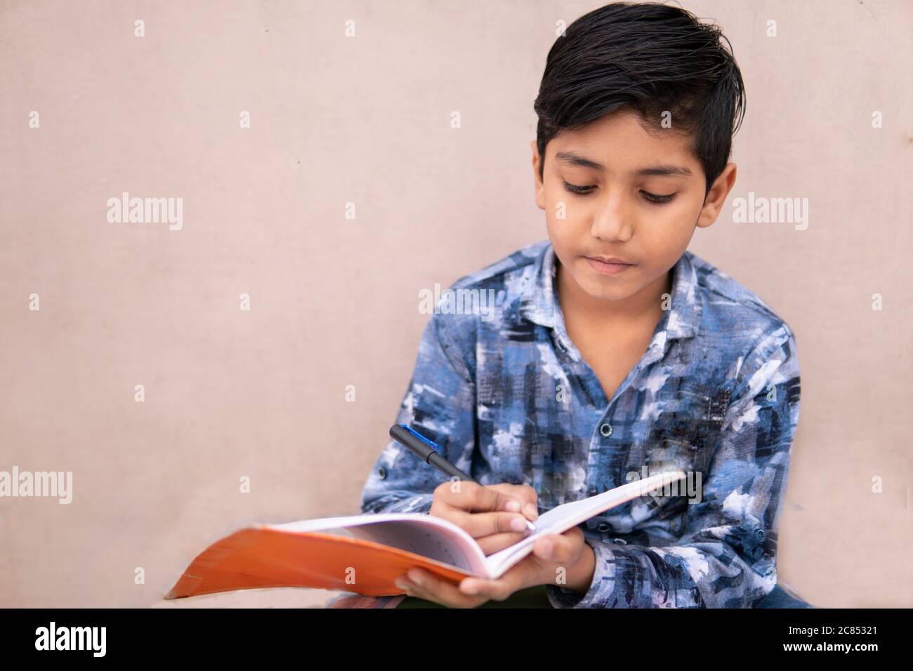 Little Indian boy student doing study at home. He is writing on ...