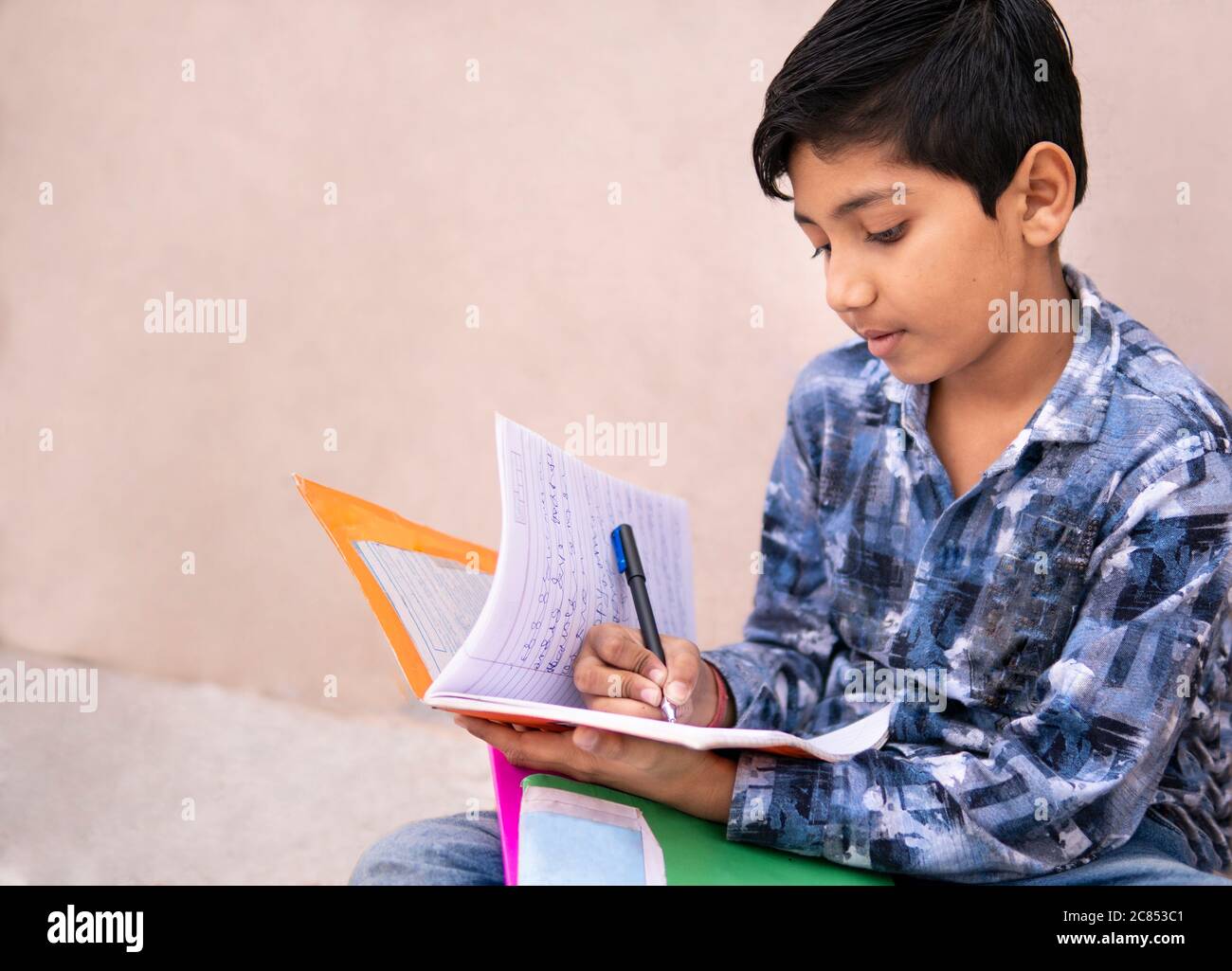 Little Indian boy student doing study at home. He is writing on ...