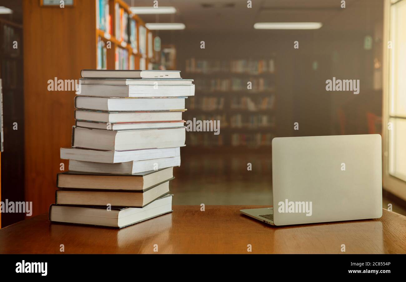 Stack of old books and laptop computer on desk in library background ...