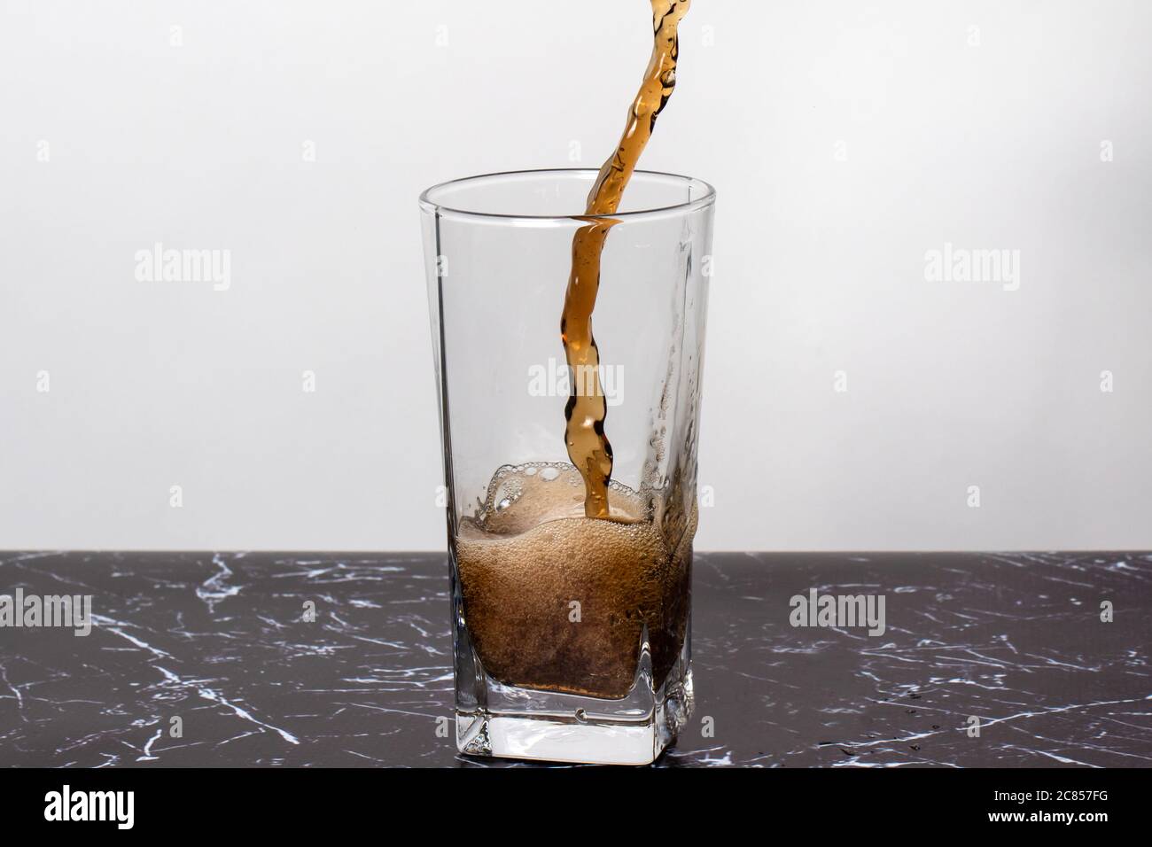 A brown dark sweet drink is poured into a glass beaker, spatter and a ...