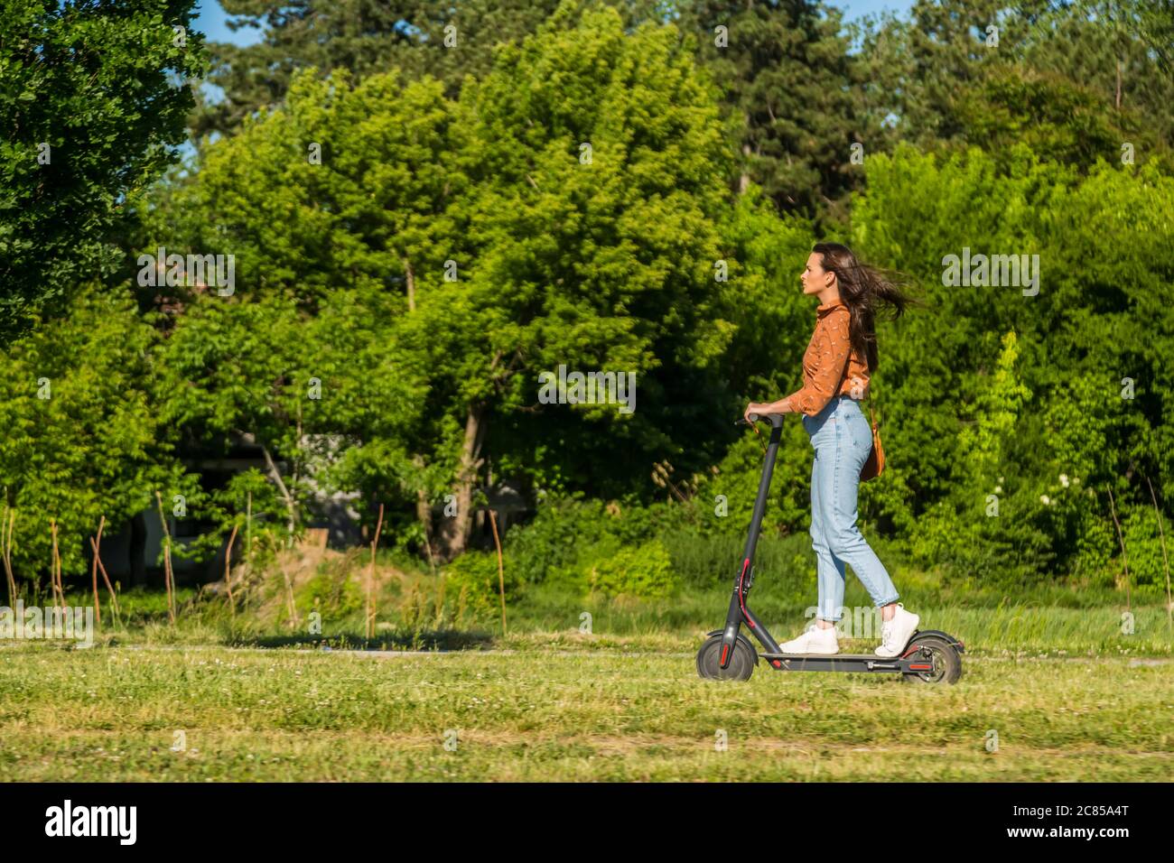 Young beautiful woman rides on an electric scooter through the park and ...