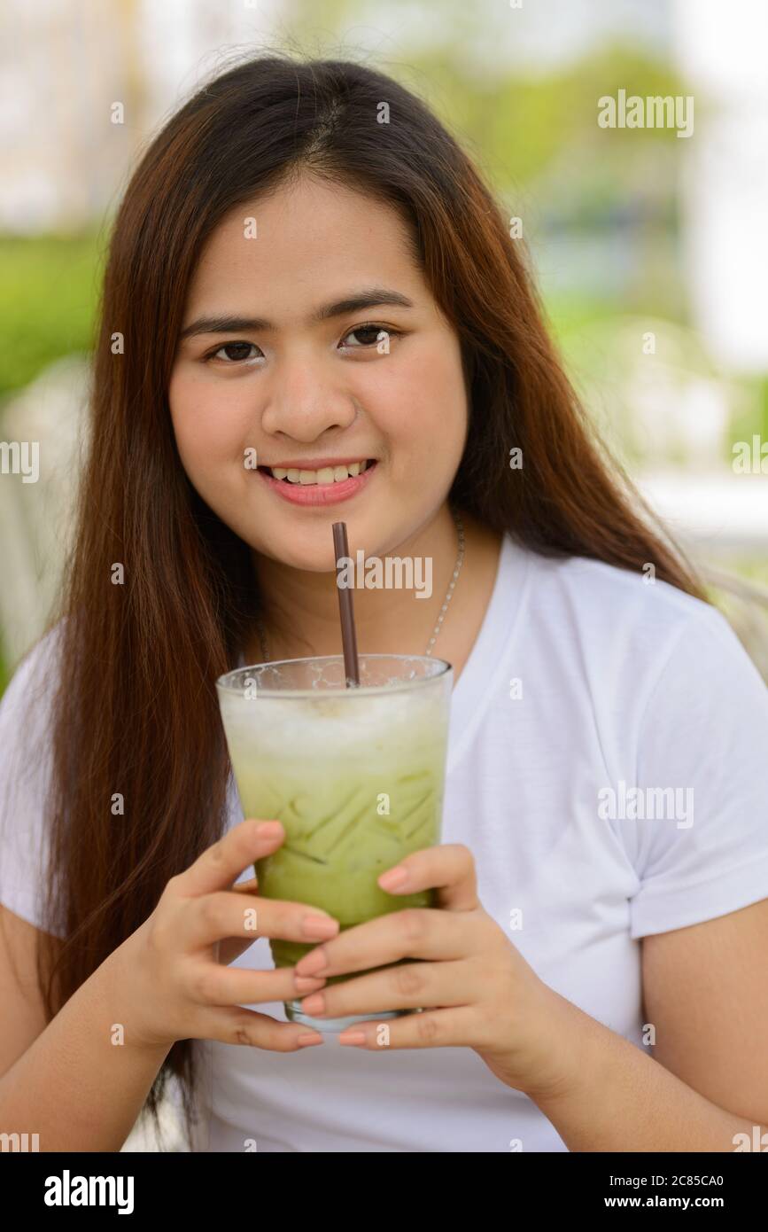 Happy young beautiful Asian woman with iced green tea at the coffee ...
