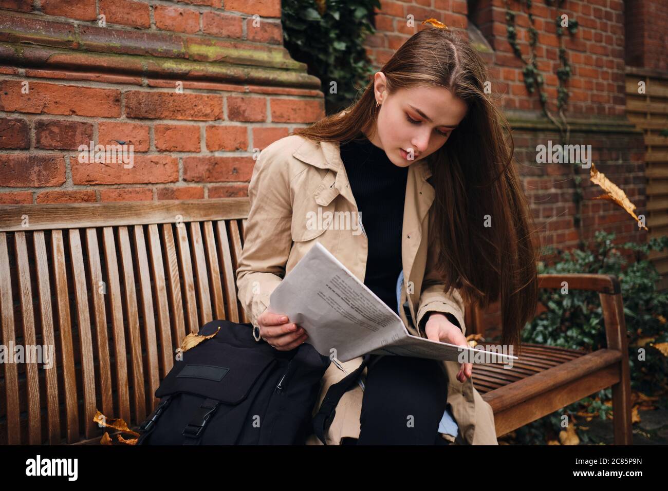 Attractive girl thoughtfully reading newspaper sitting with backpack on ...