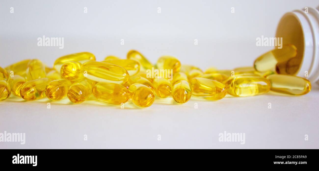 White vial with yellow vitamins tablets, fish oil, Omega Vitamin E ...