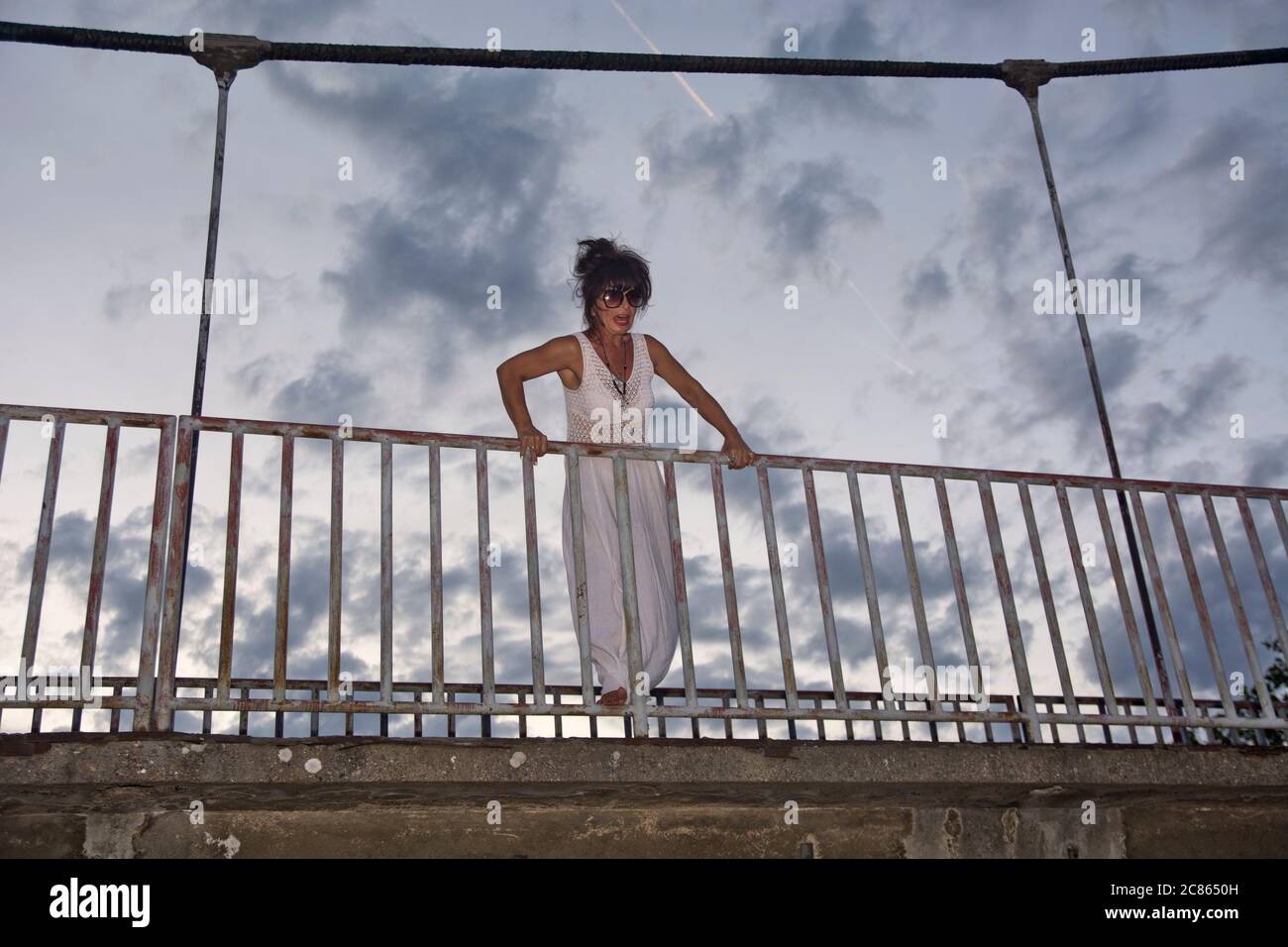An attractive female model poses on a fence from the footpath of a ...