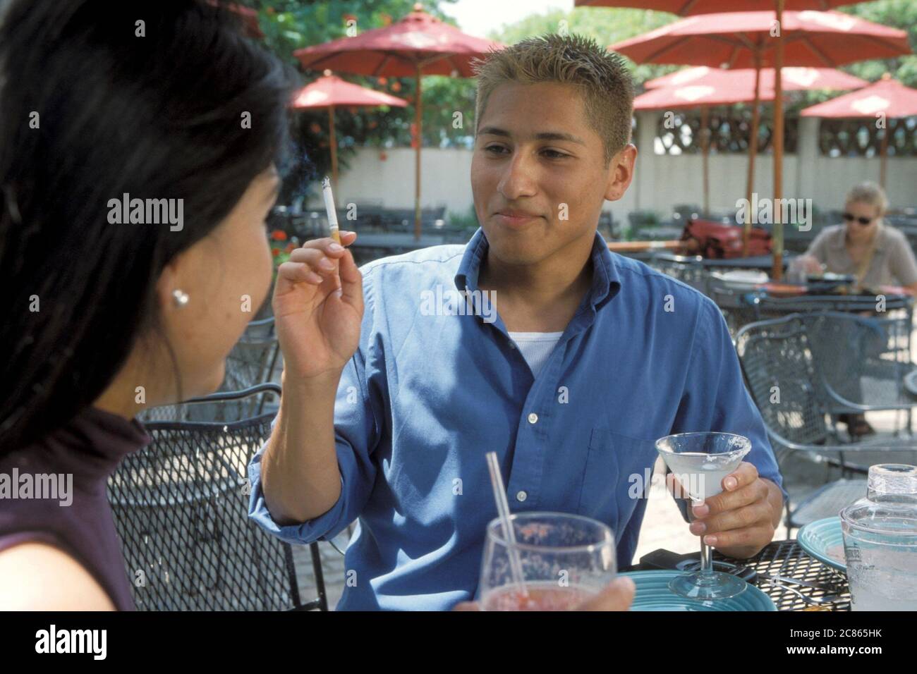 Austin Texas USA, 2003: Mid-20's Hispanic man smokes cigarette in outdoor smoking section at ...