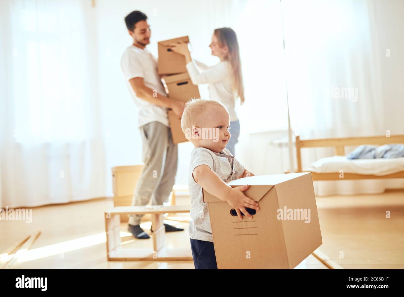 Happy little boy carrying moving box, parents on blurred background ...