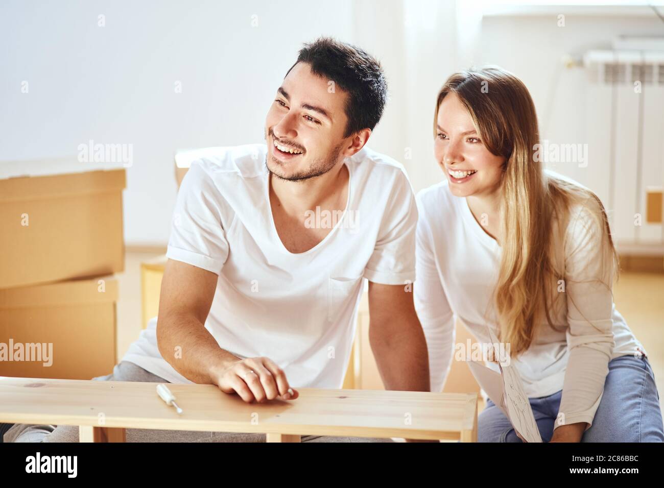 Couple assembling furniture in new home, cardboard moving boxes on ...