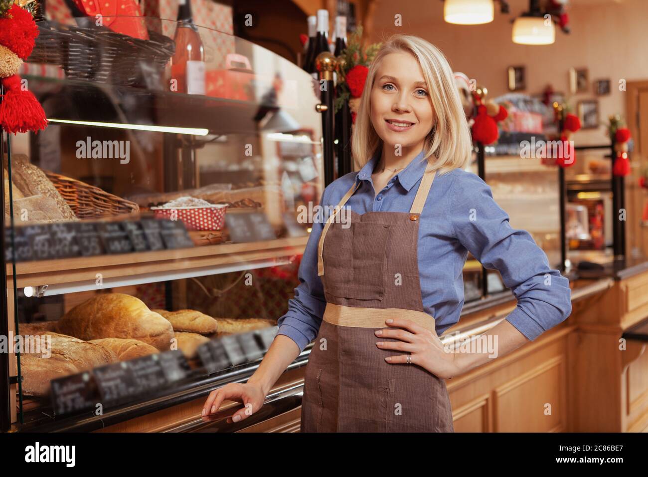 Happy beautiful female baker posing proudly at her bakery store, copy ...