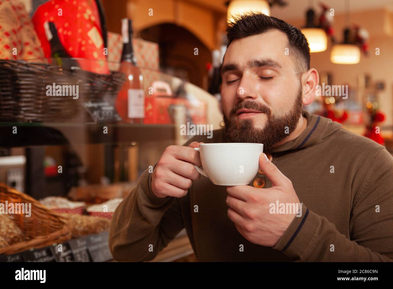 Happy bearded young man enjoying smell of fresh coffee, having ...