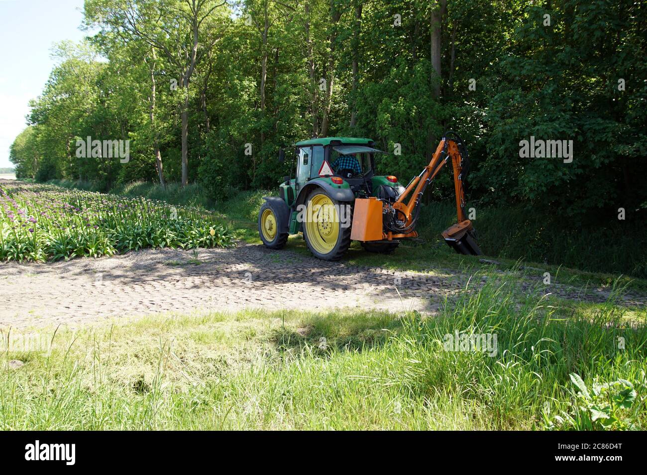 With the tractor the grass is cut on the slope of a ditch with a row of ...