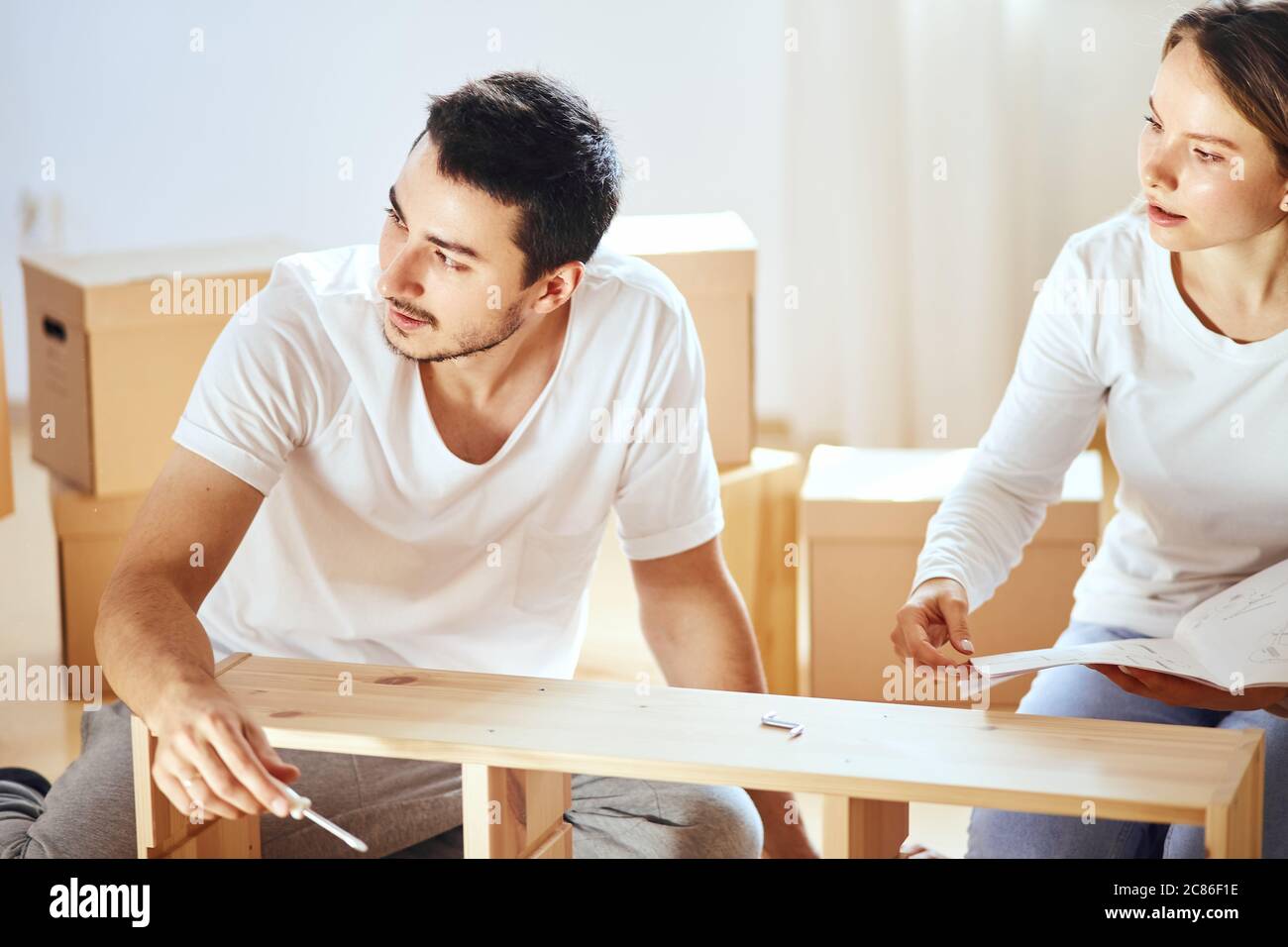 Couple assembling furniture in new home, cardboard moving boxes on ...