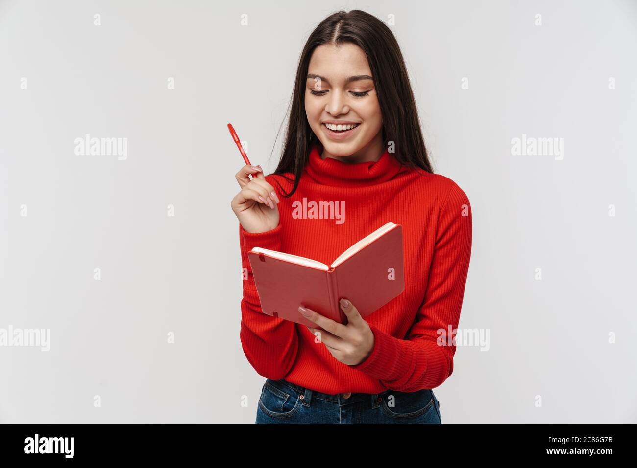 Photo of happy caucasian cute woman smiling and making notes in planner ...