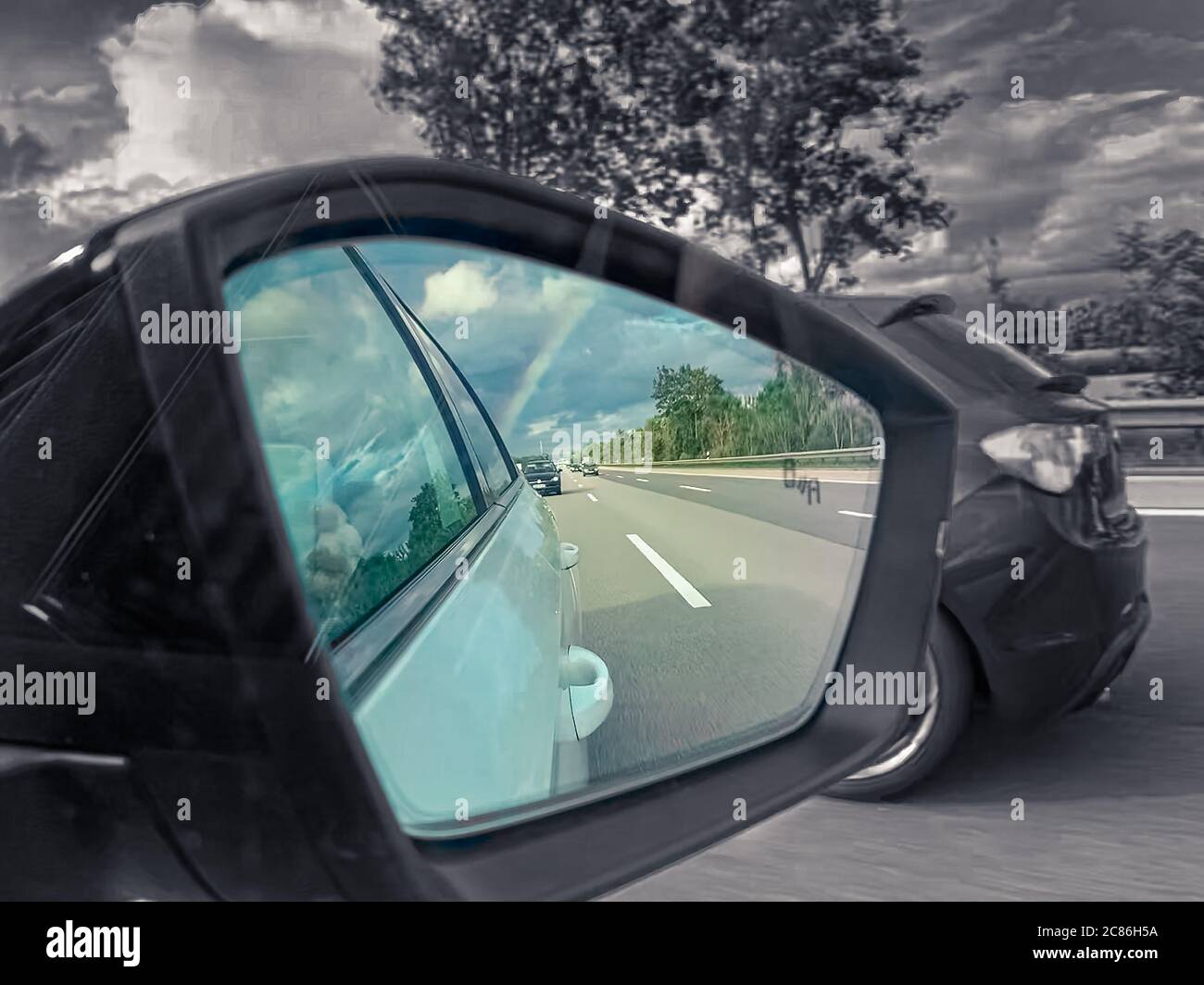 rearview car driving mirror view at a colorful rainbow while the ...
