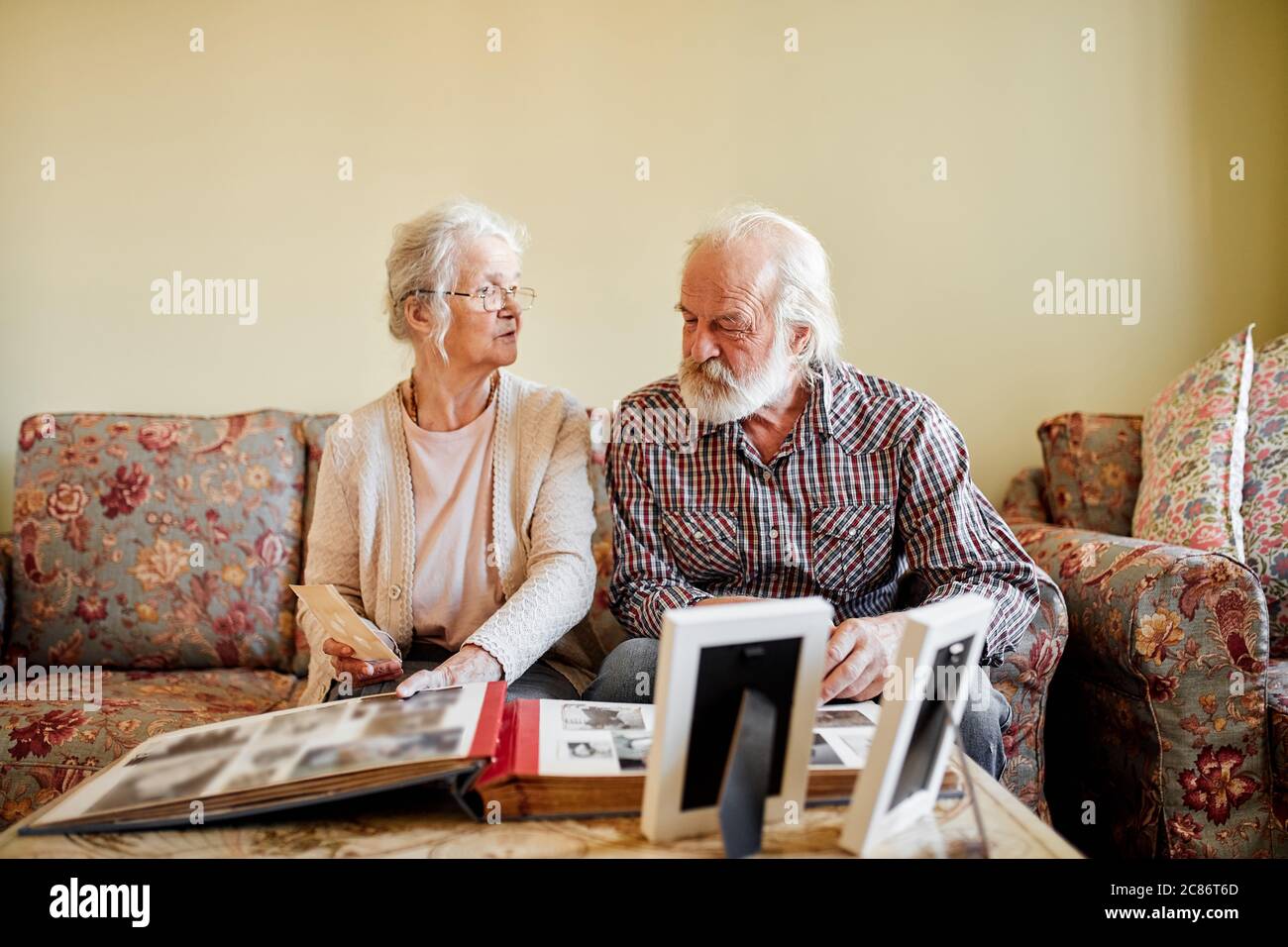 Senior bearded man sitting on the sofa with his old-aged wife looking ...