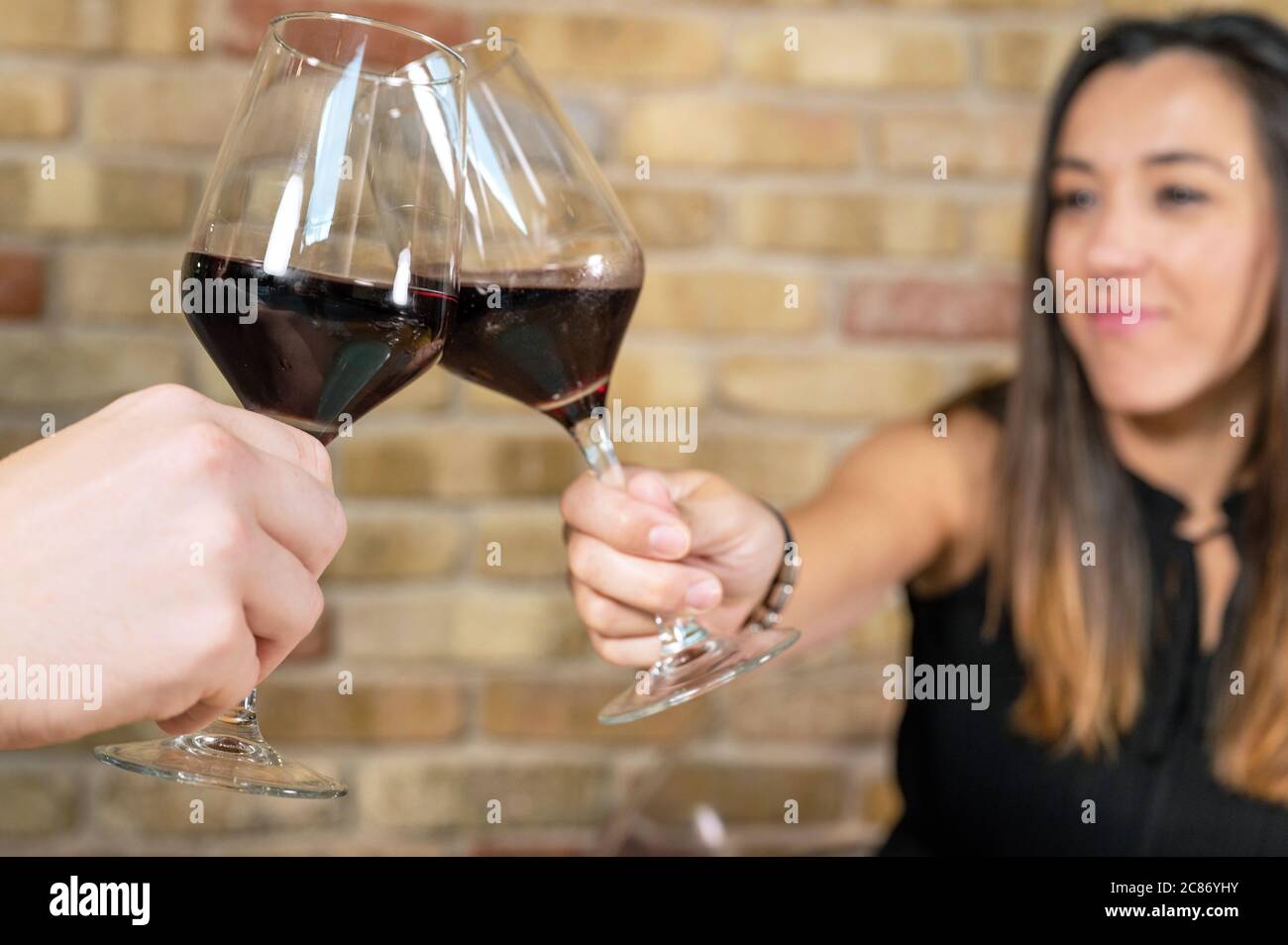 Close up of young couple toasting with glasses of red wine at ...