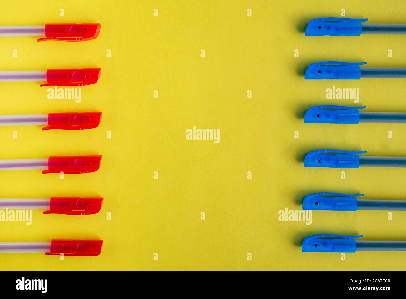 Blue and red ballpoint pens on a yellow background opposite each other ...
