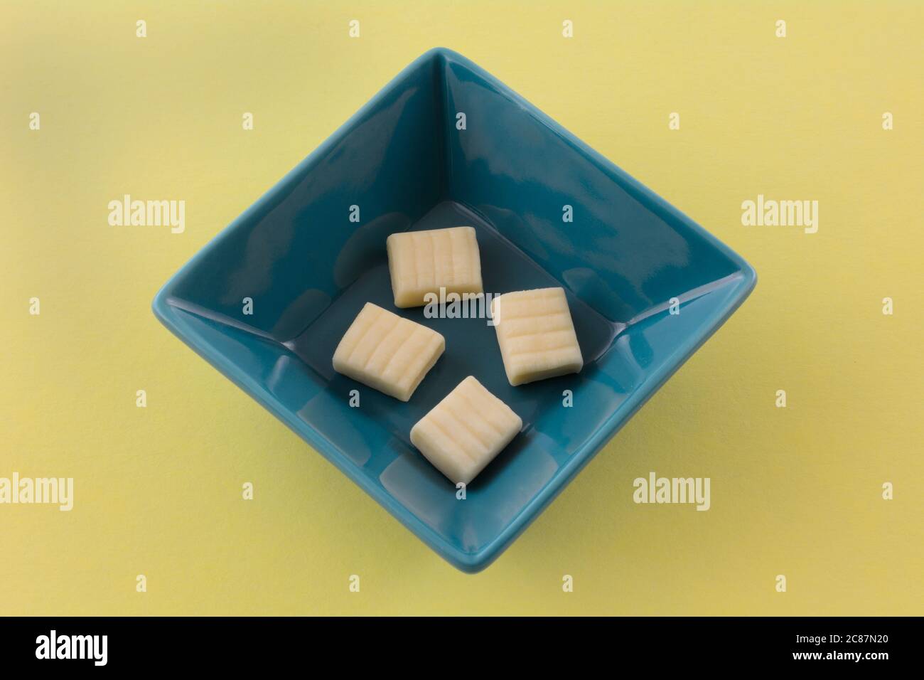 Sweet corn flavored hard candy chews in blue candy dish on yellow ...