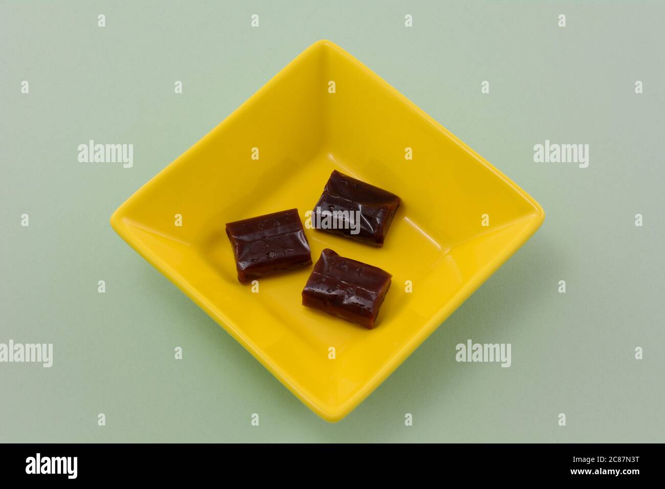 Banana chew candy pieces in yellow candy dish on green background Stock ...