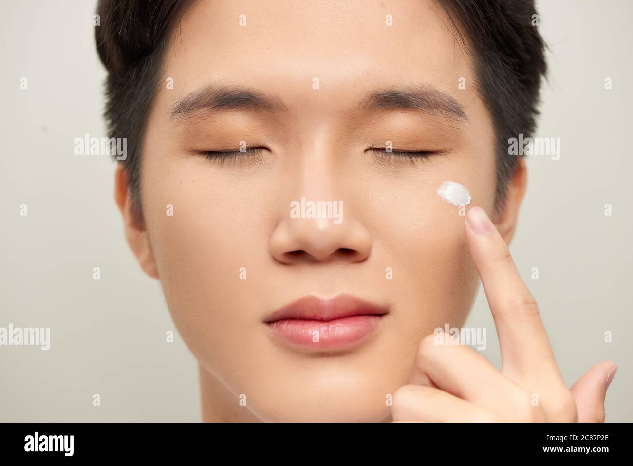 Portrait of satisfied young man applying facial cream isolated over ...