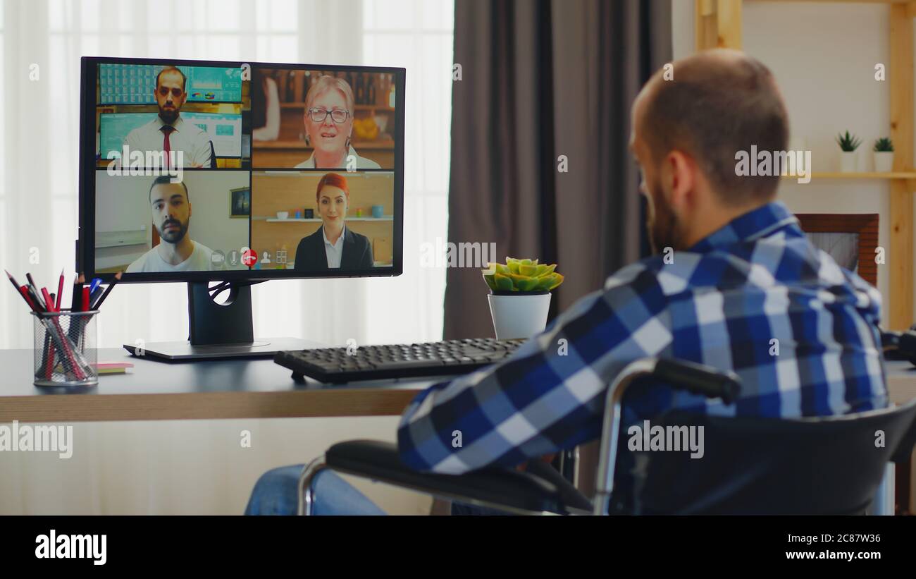 Invalid man in wheelchair greeting people during a video call working ...