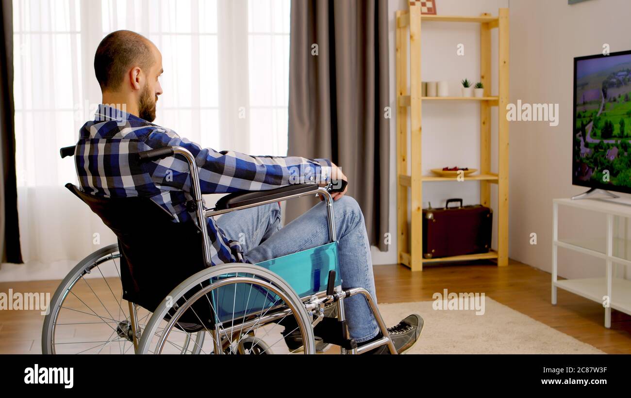 Thoughtful paralyzed man in wheelchair watching tv Stock Photo - Alamy