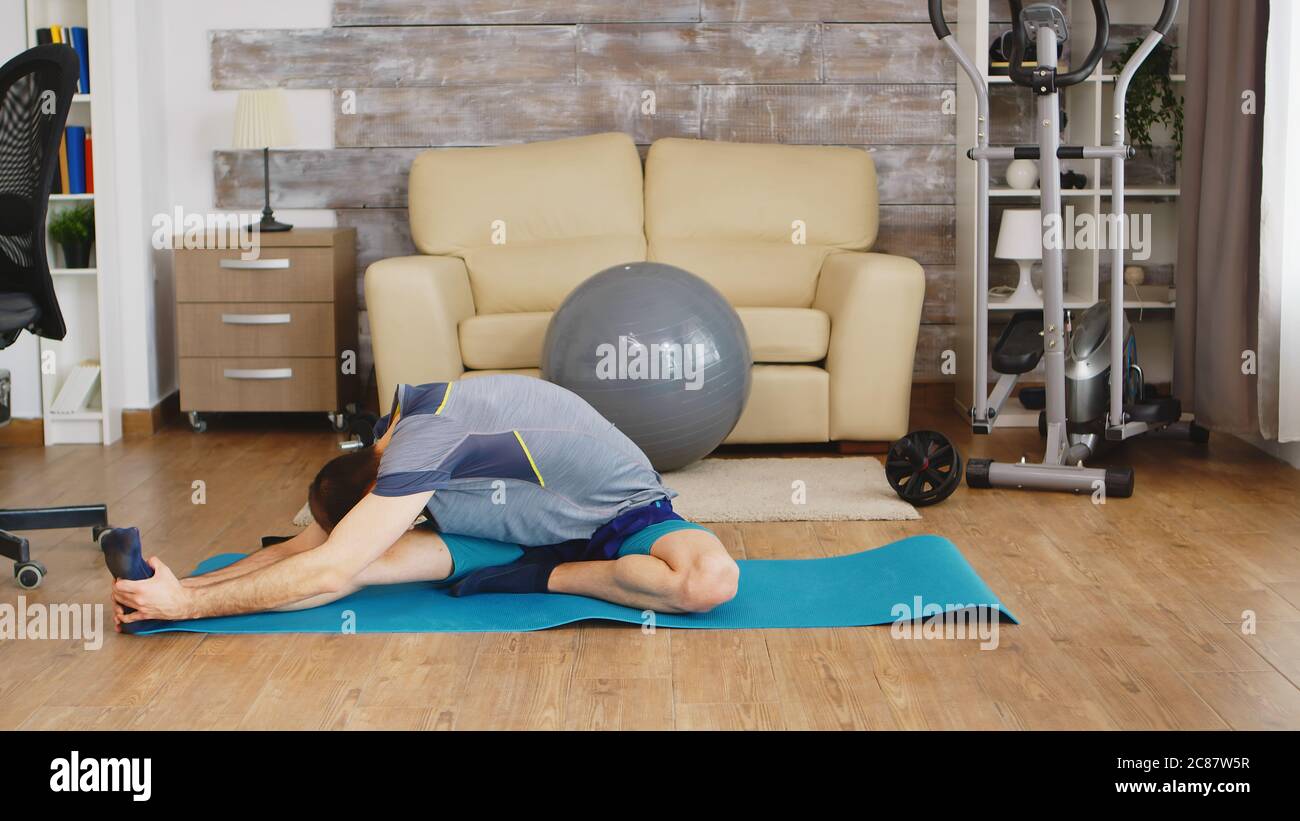 Man on yoga mat stretching his body before working out in living room ...