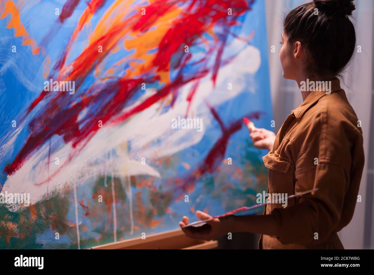 Professional woman painter looking at painting and holding paint ...