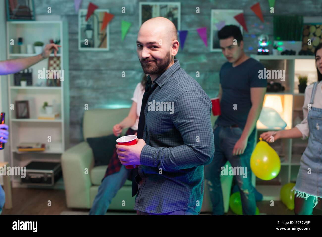 Bald man looking at the camera at a party his friends while partying ...