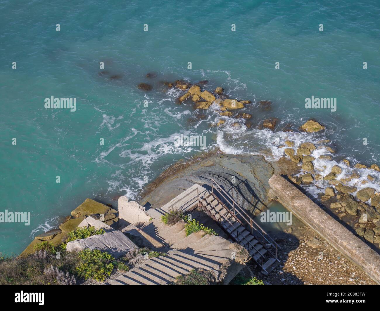 concrete steps on a steep slope leading to the rocky blue sea shore ...