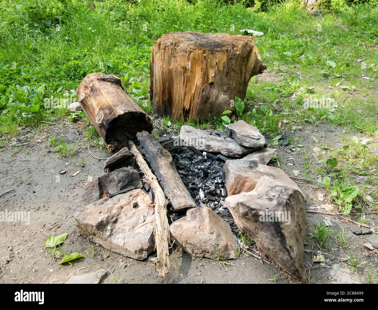Stone camp fire pit with a log or stub for sitting down . Burnt wood in ...