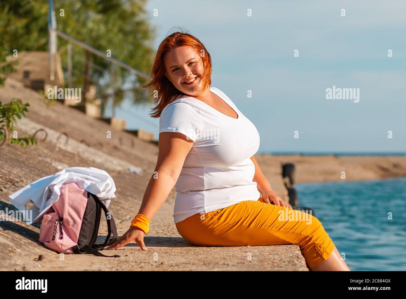 Portrait of a happy overweight woman poses while sitting on a sea pier ...
