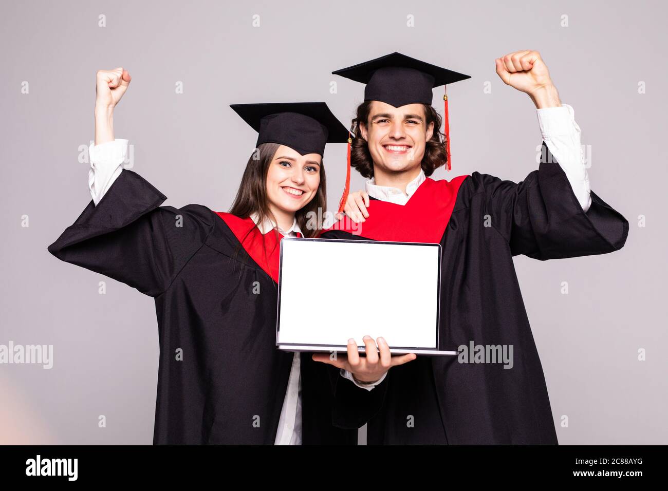 Young graduation couple holding laptop isolated on white background ...