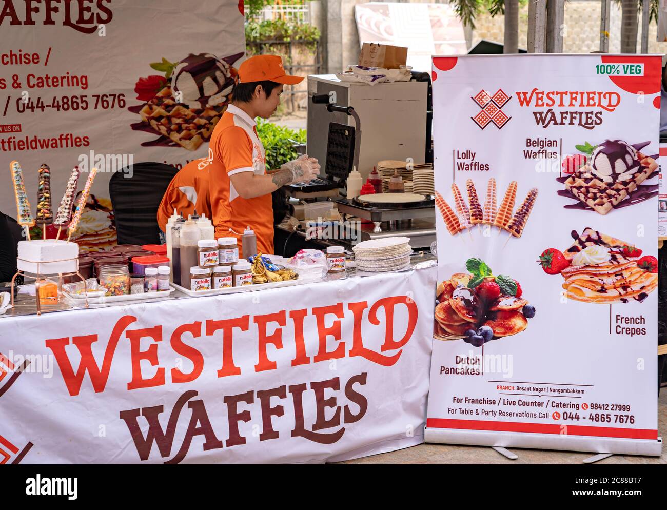 An employee working at a food stall serving waffles, crepes, and ...