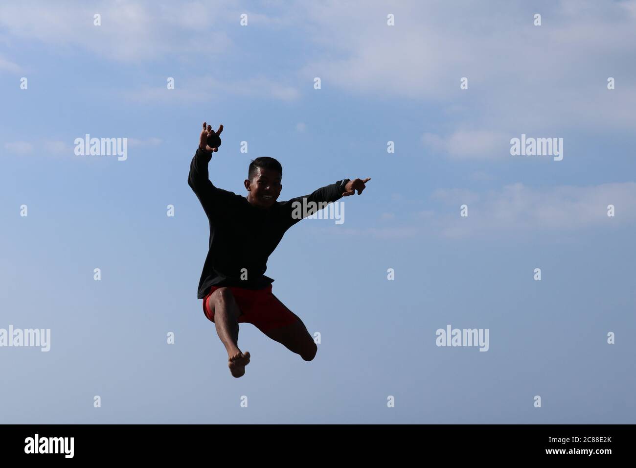 Happy man jumping. Blue sky background. Young cheerful Indonesian boy ...