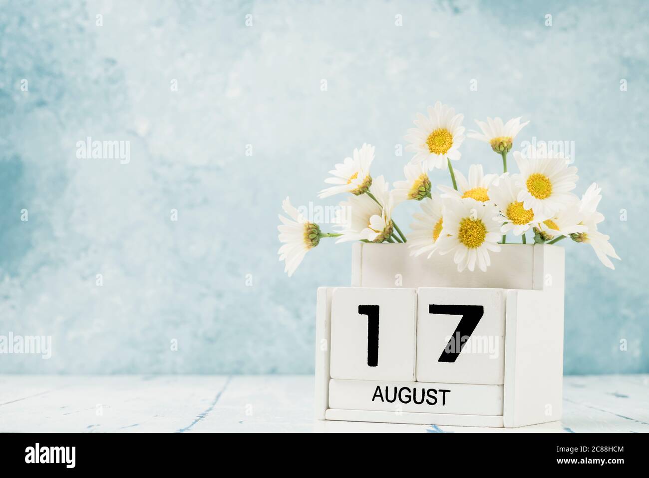 White cube calendar for august decorated with daisy flowers over blue ...