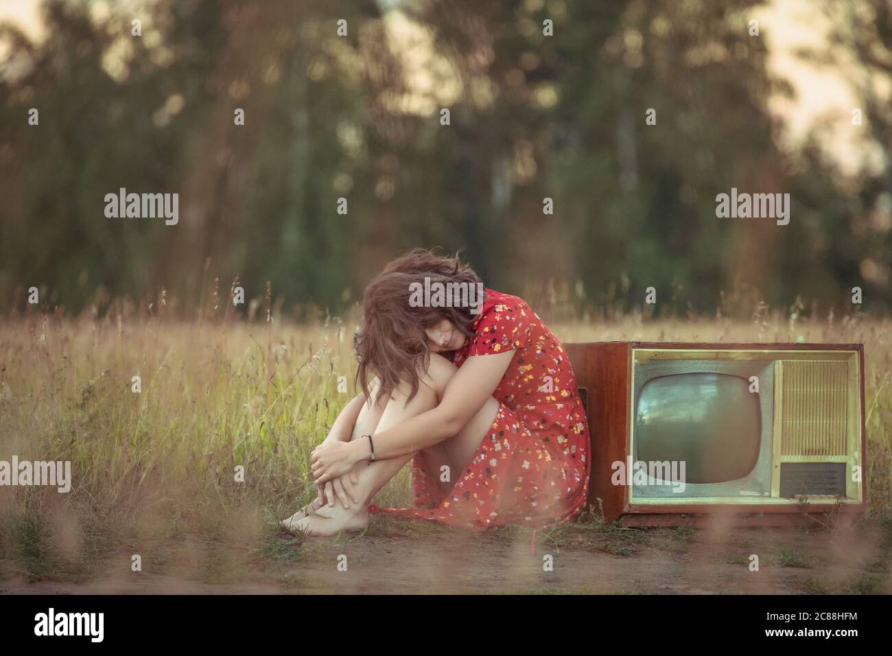 Atmospheric portrait of a brooding young woman in a red dress sitting ...