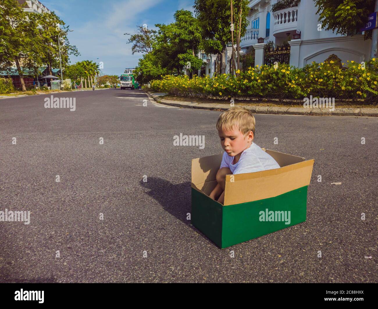 Cute little child boy sitting inside cardboard box on silent street in ...