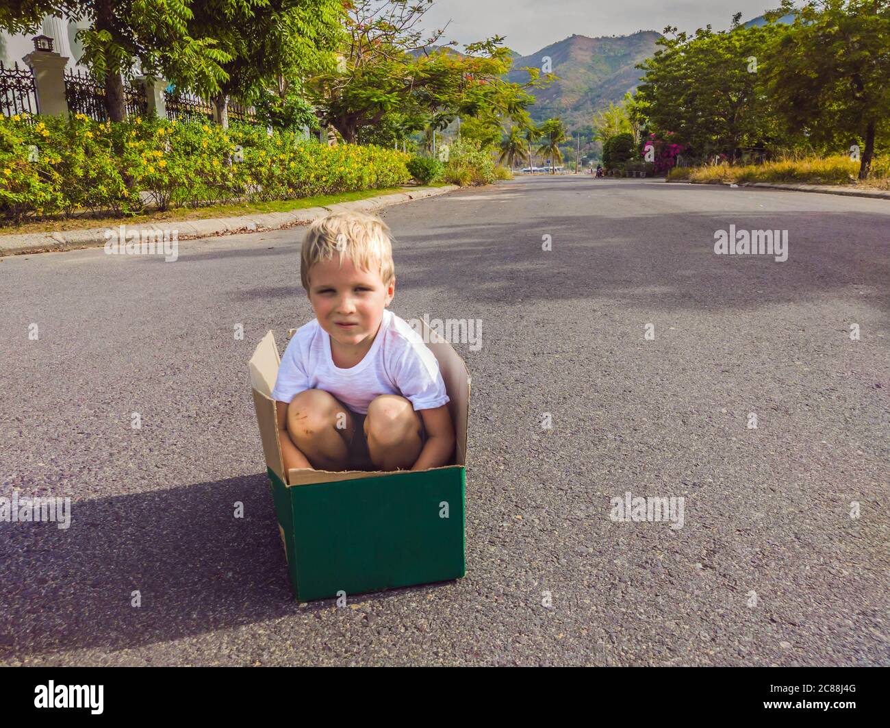 Cute little child boy sitting inside cardboard box on silent street in ...