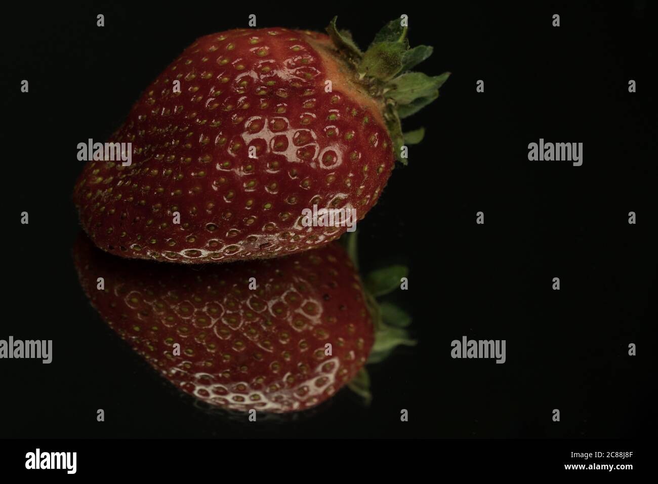 A tasty red ripe strawberry on a mirror. Isolated close-up detail shot ...