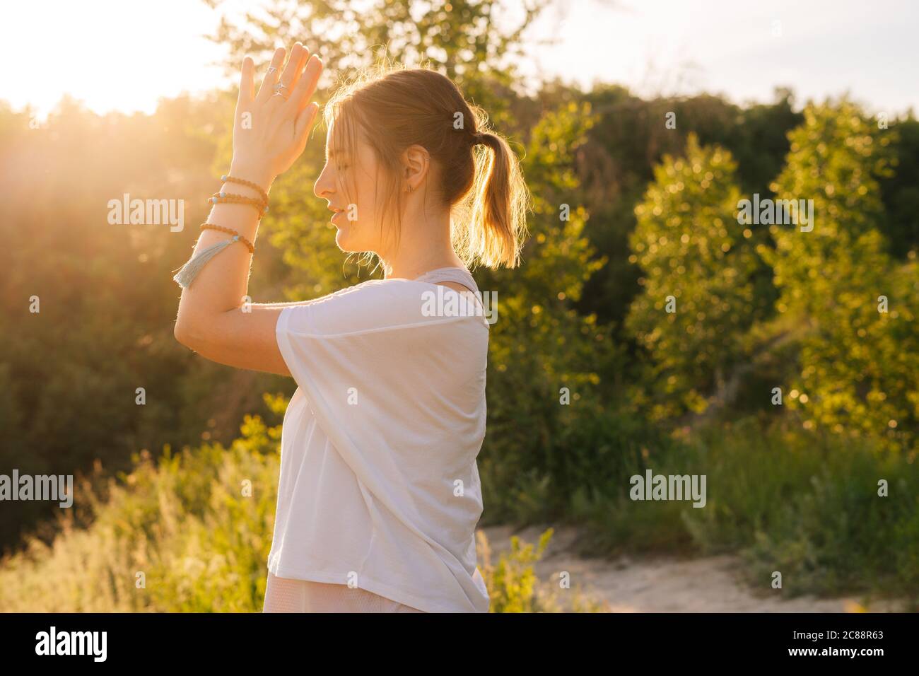 Side view of happy meditating woman raising hands in Namaste pose ...