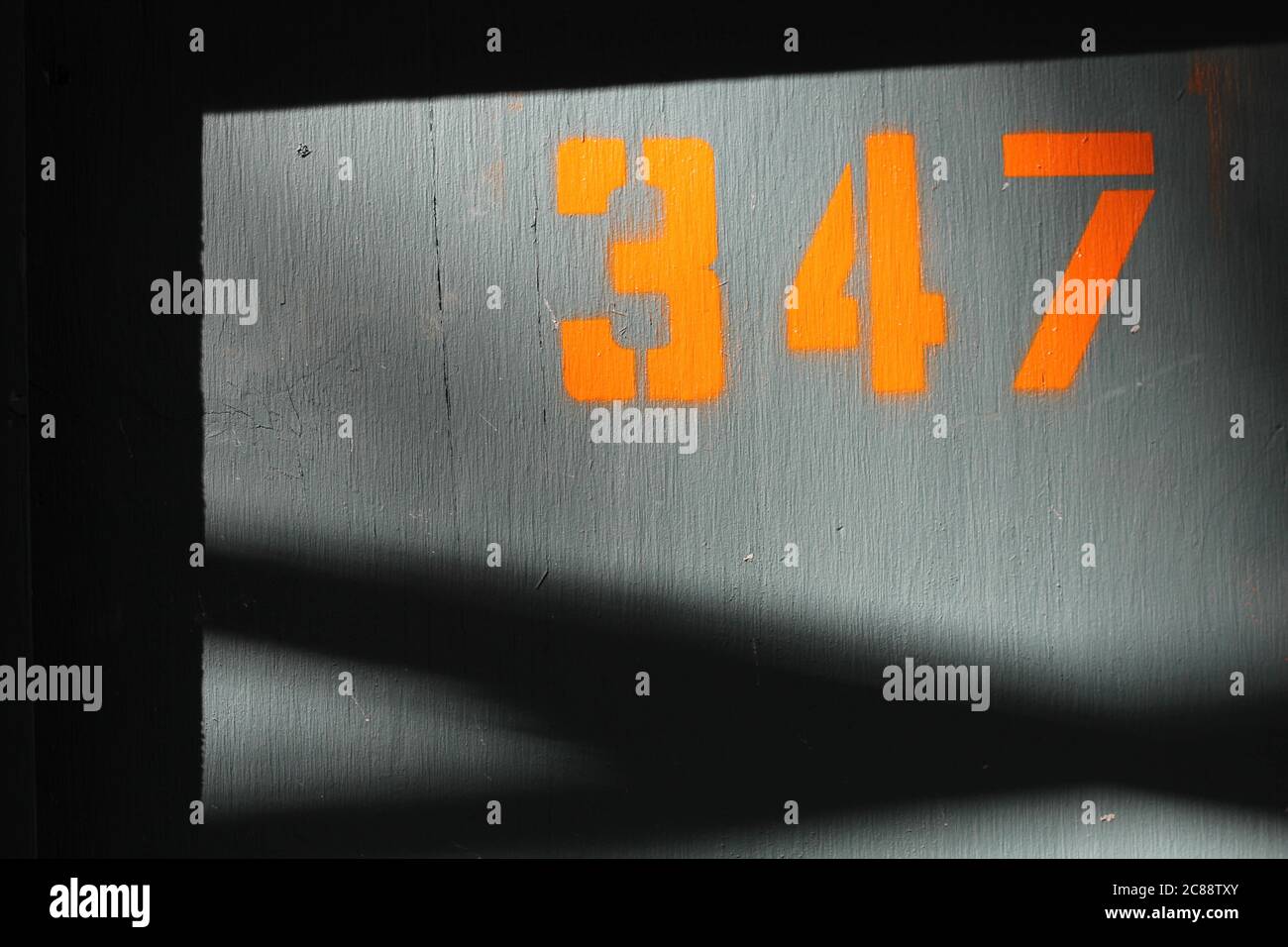Grey wooden wall and the number 347 written on it with bright orange ...